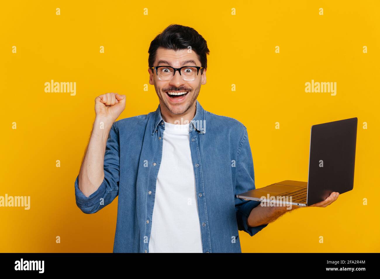 Happy young intelligent man with glasses, holds an open laptop in his ...