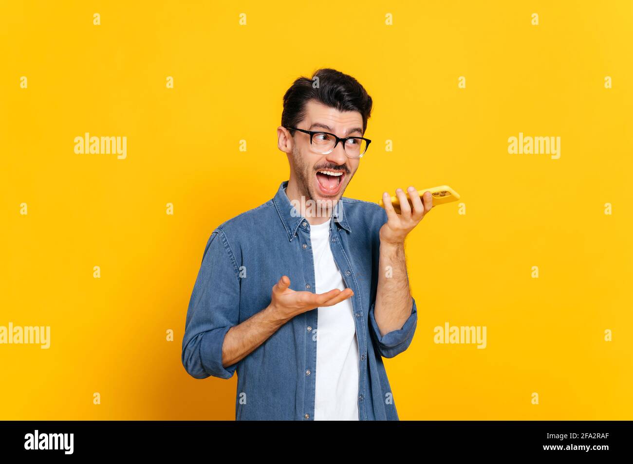 Emotional caucasian stylish guy with glasses, holding smartphone in ...