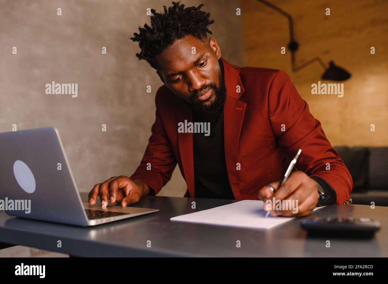 a focused black man in a suit is working on a laptop. Remote work from ...