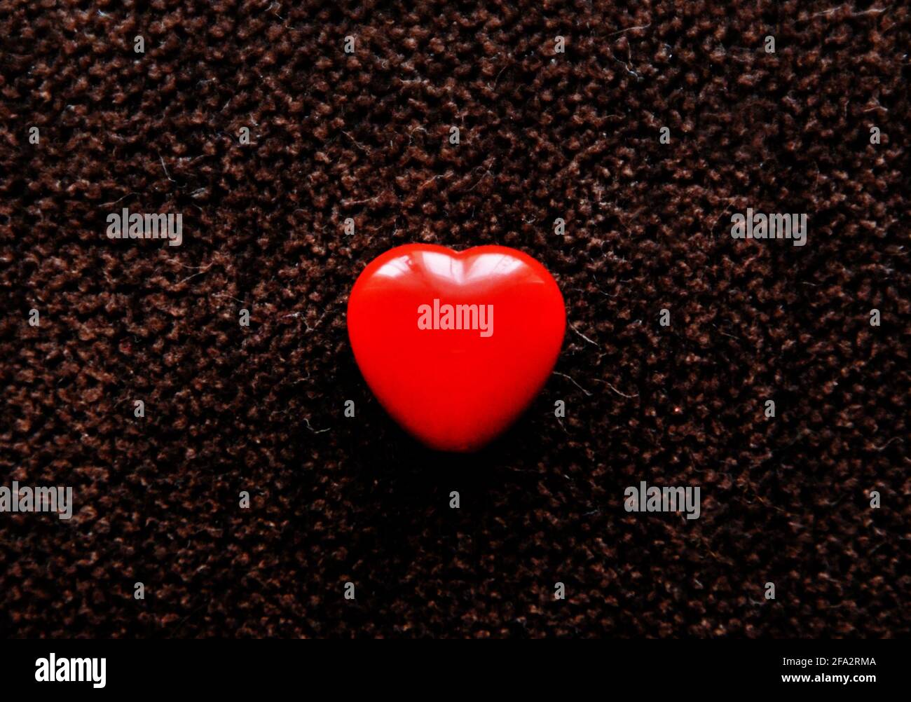 Red heart-shaped pin at the midpoint of a brown textured fabric Stock ...