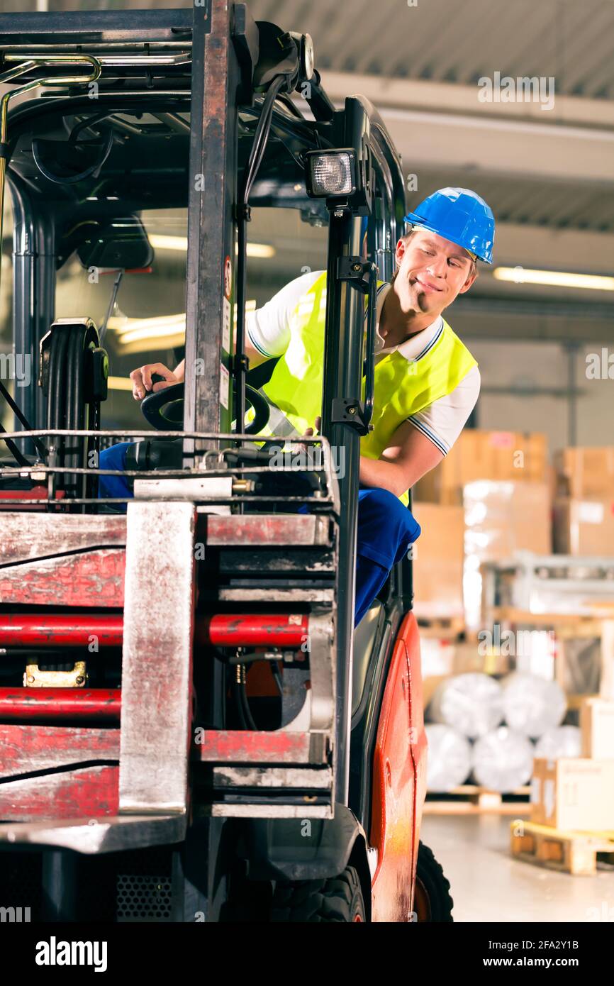 forklift driver in protective vest driving forklift at warehouse of ...