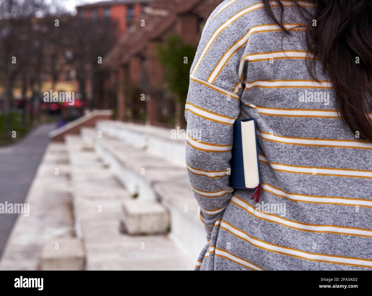 Back view of woman walking outdoors with a book under her arm. With ...