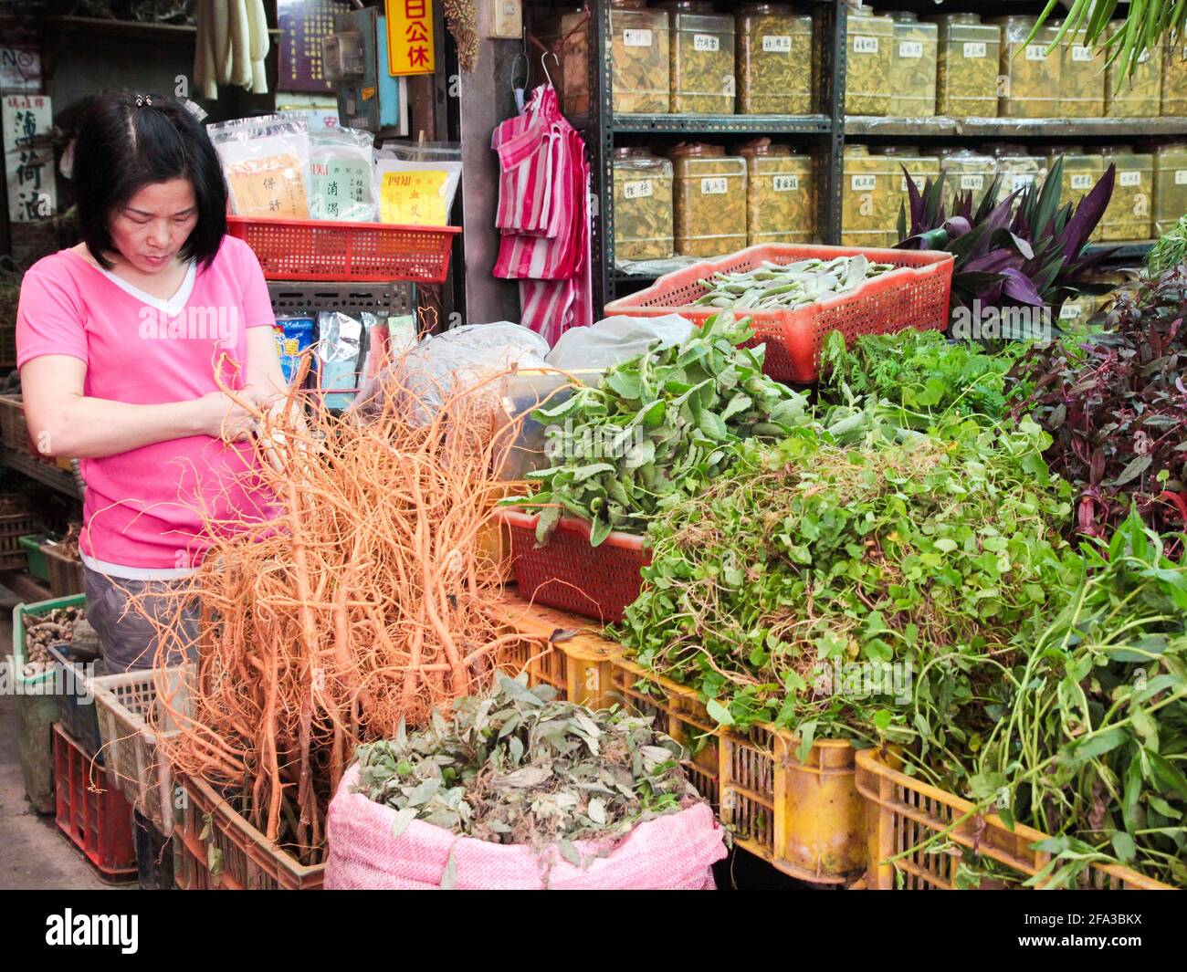 A woman working at a typical stall with roots, greens, other herbs and ...