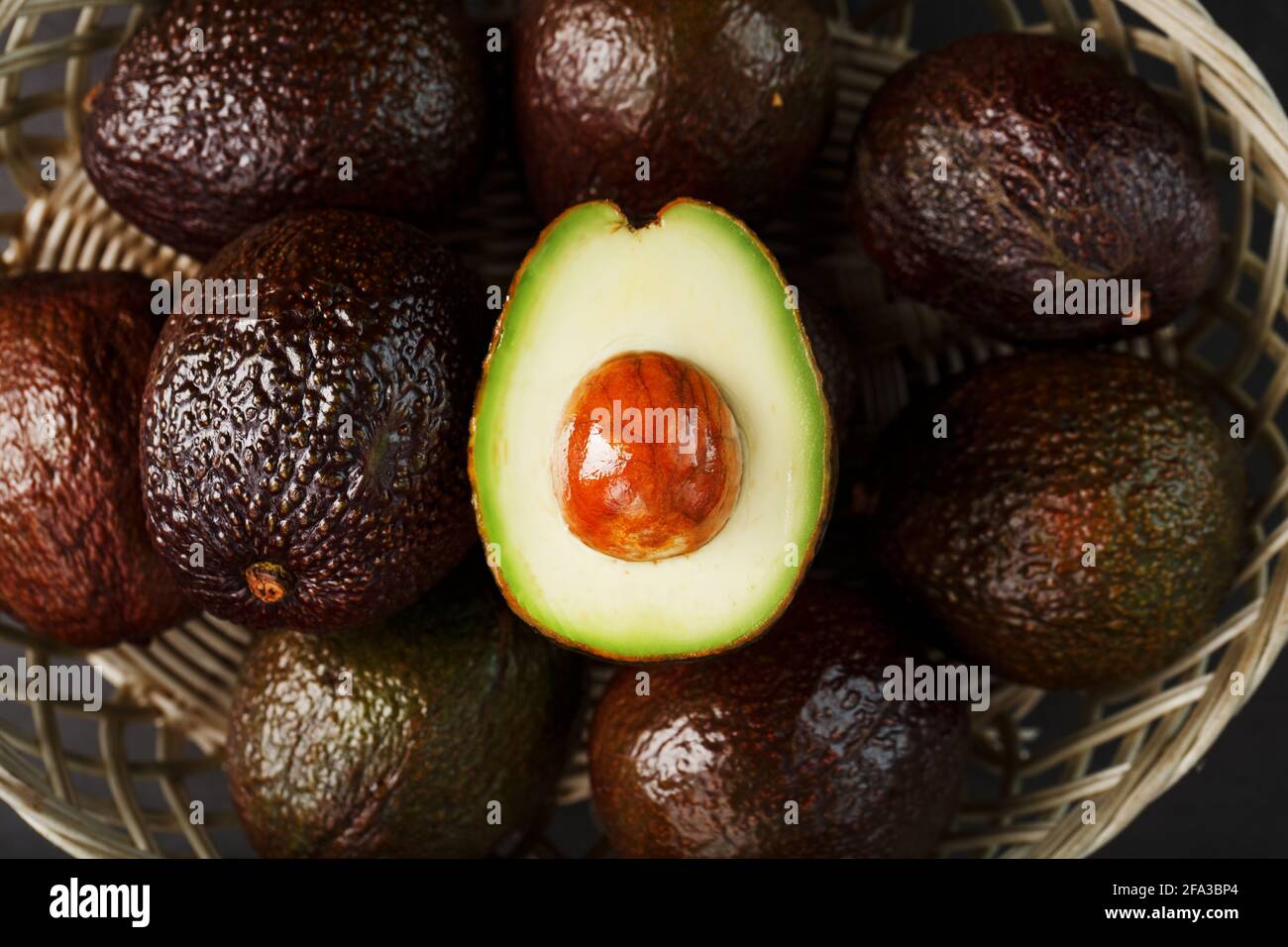 Ripe avocados in a basket on a black table, with a cut fruit and a ...