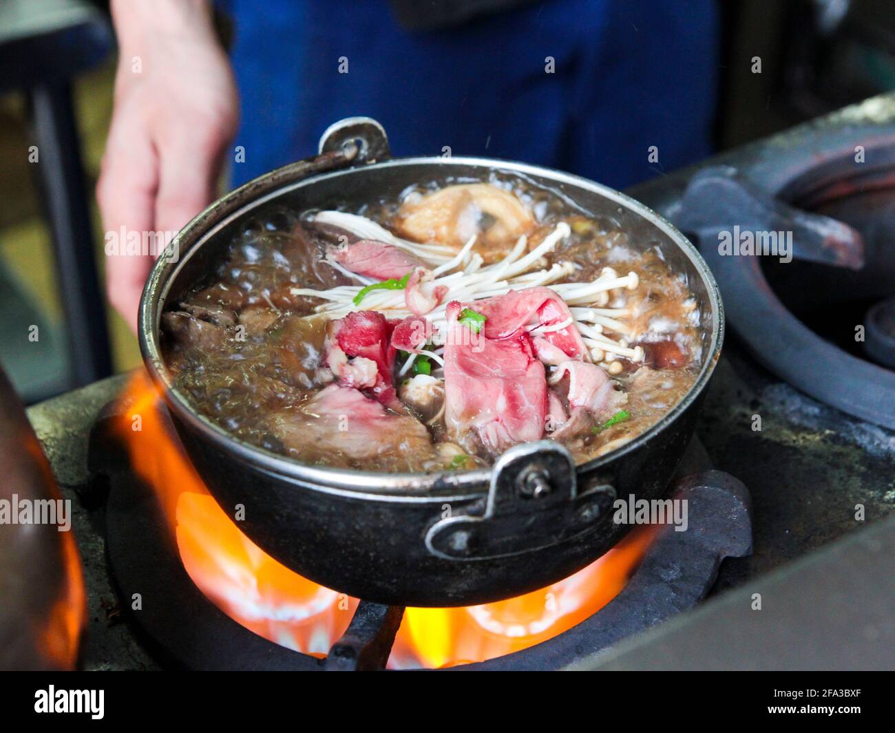 A savory soup with meat and mushrooms cooking over an open flame at a ...