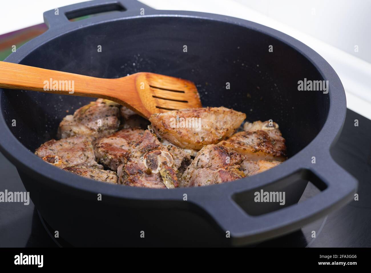 Meat being cooked in a black pot with wooden utensil. Cooking concept ...