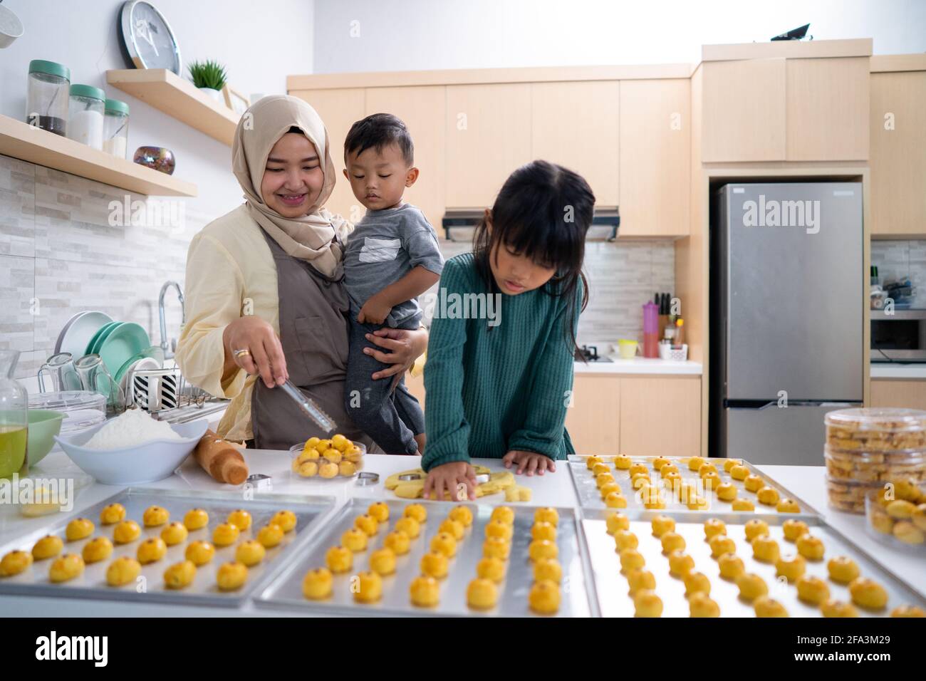young muslim woman with two her children cooking in the kitchen ...