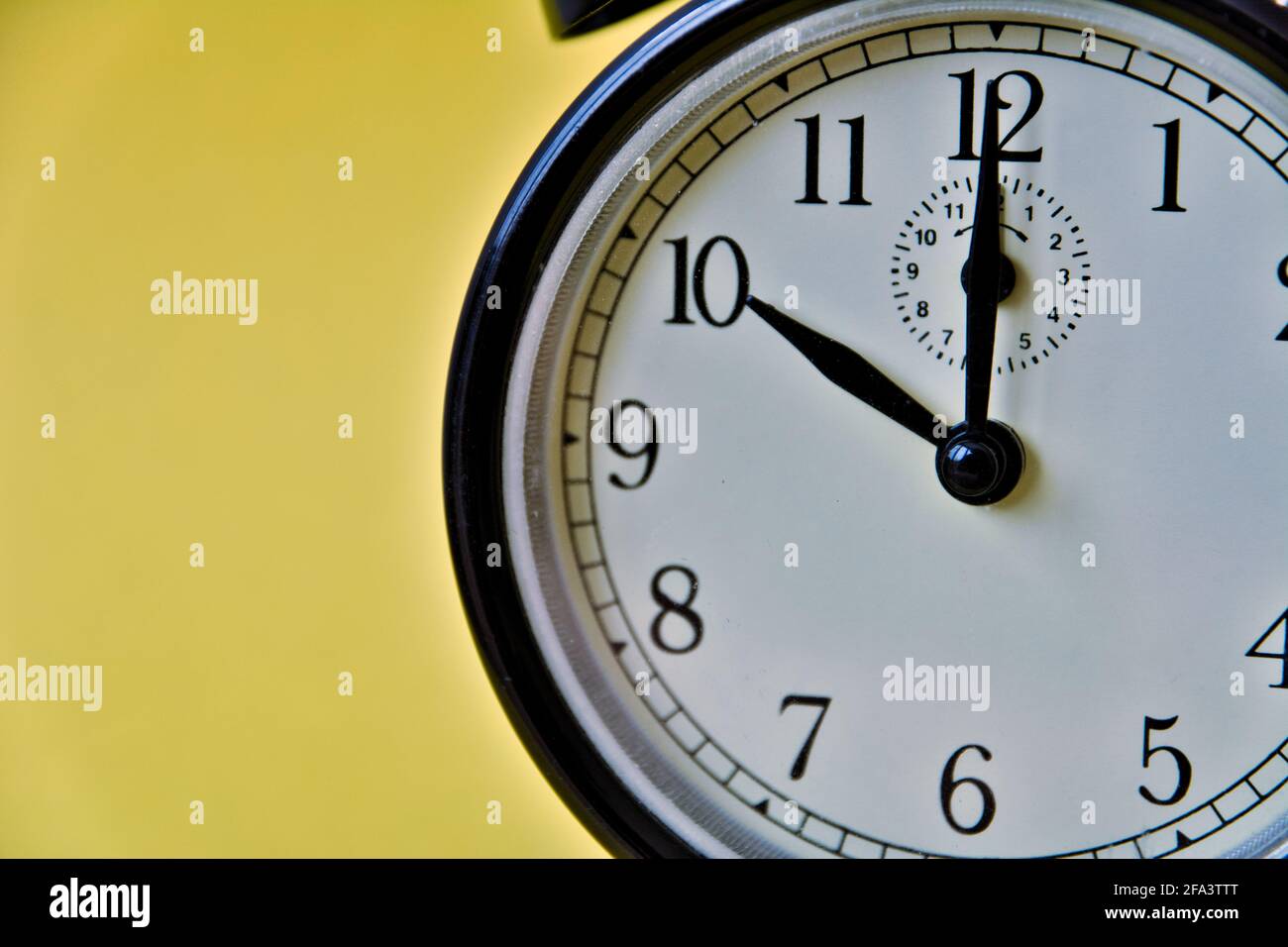 Shot of vintage retro analog clock on yellow background showing 10 o ...
