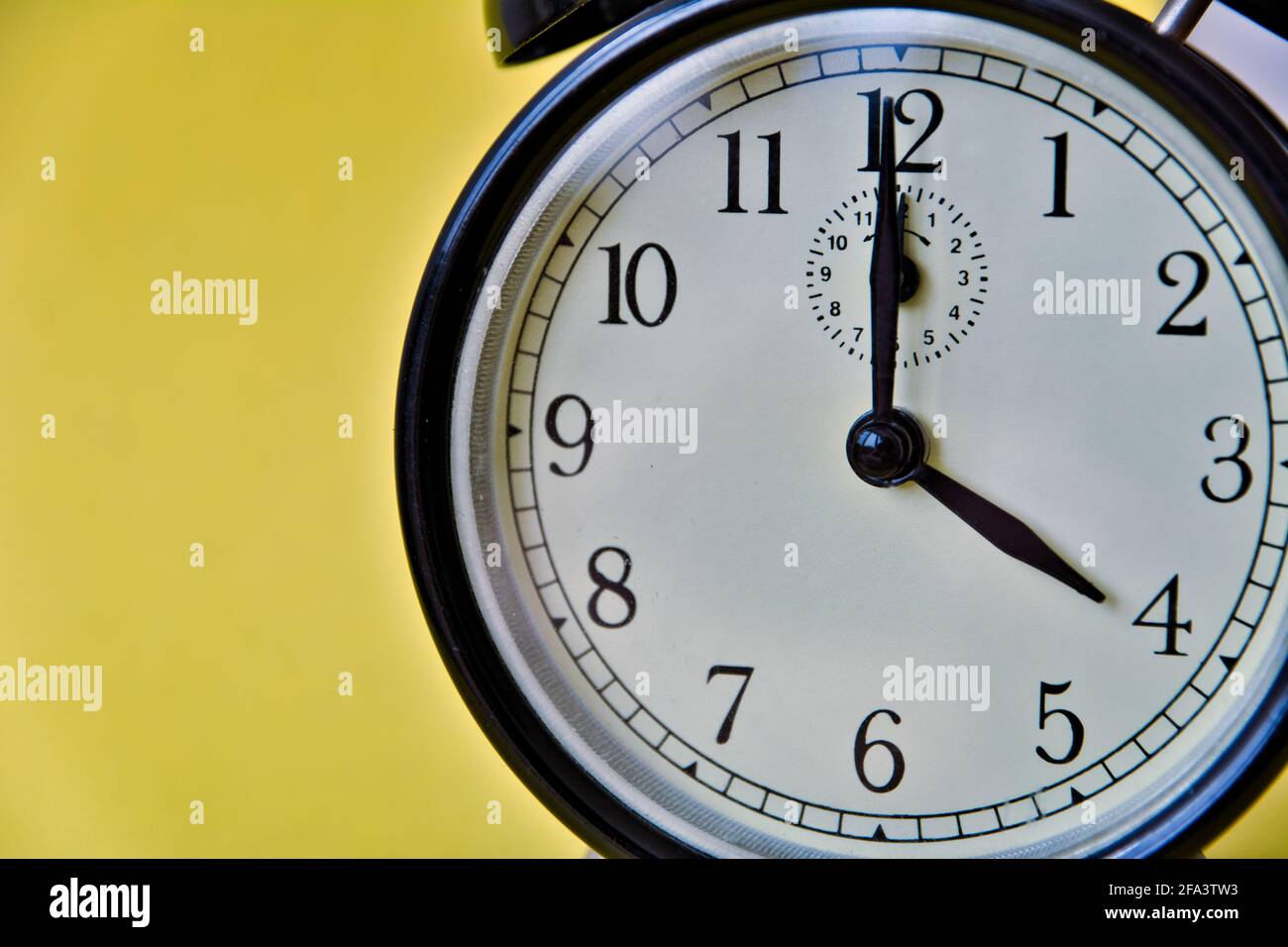 Shot of vintage retro analog clock on yellow background showing 4 o ...