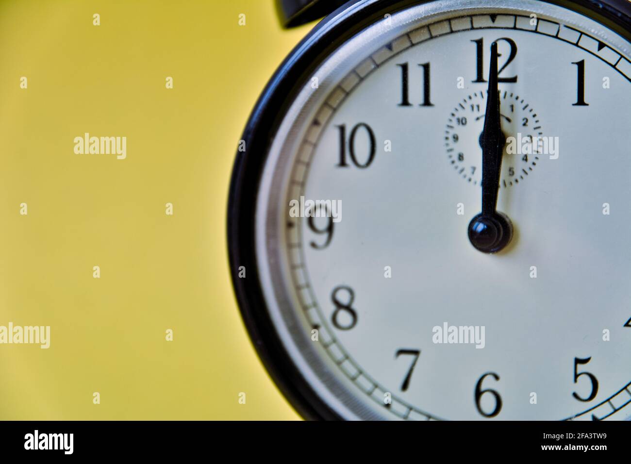 Shot of vintage retro analog clock on yellow background showing 12 o ...