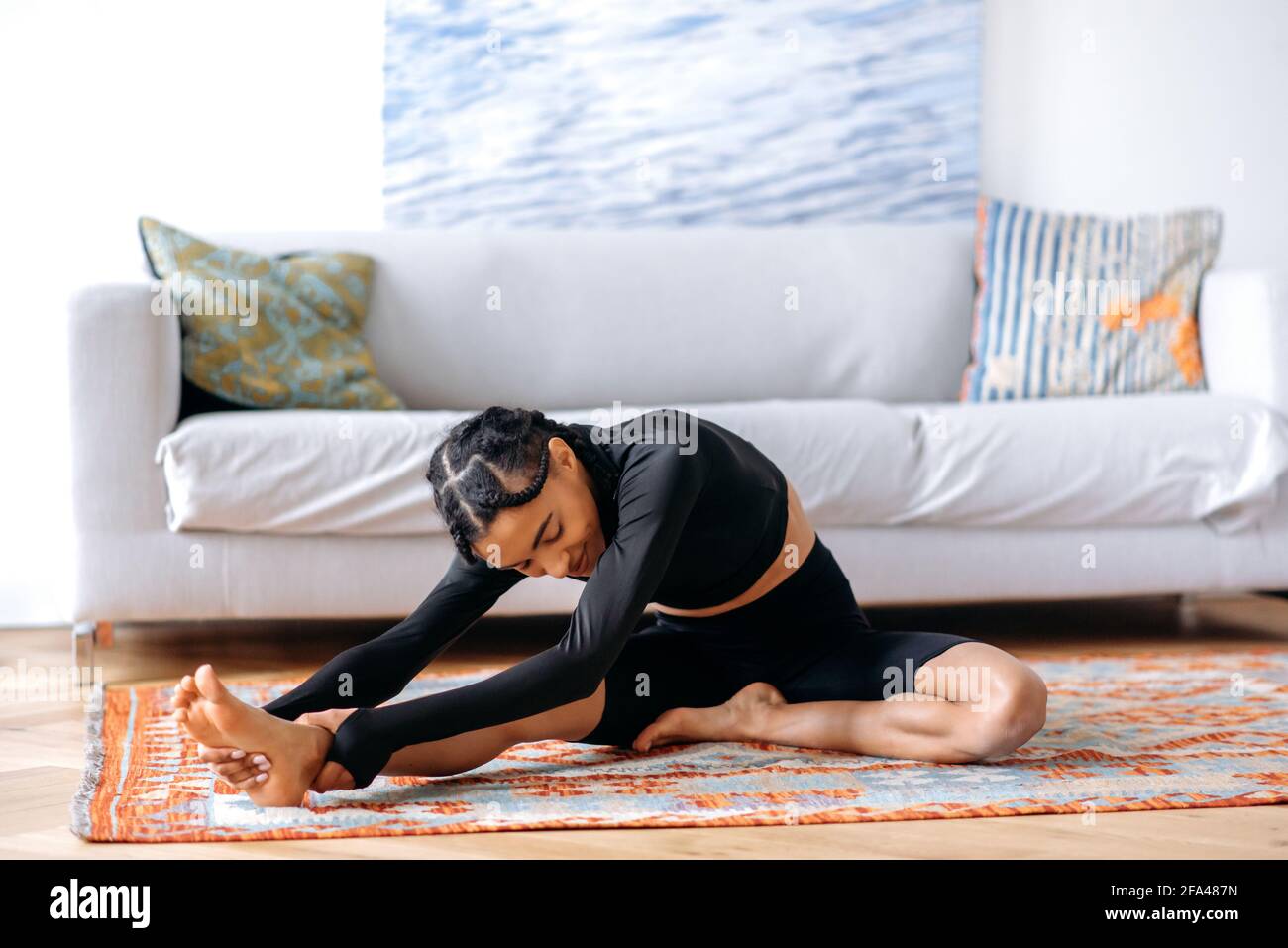 Flexible athletic young African American woman in sportswear, at home ...