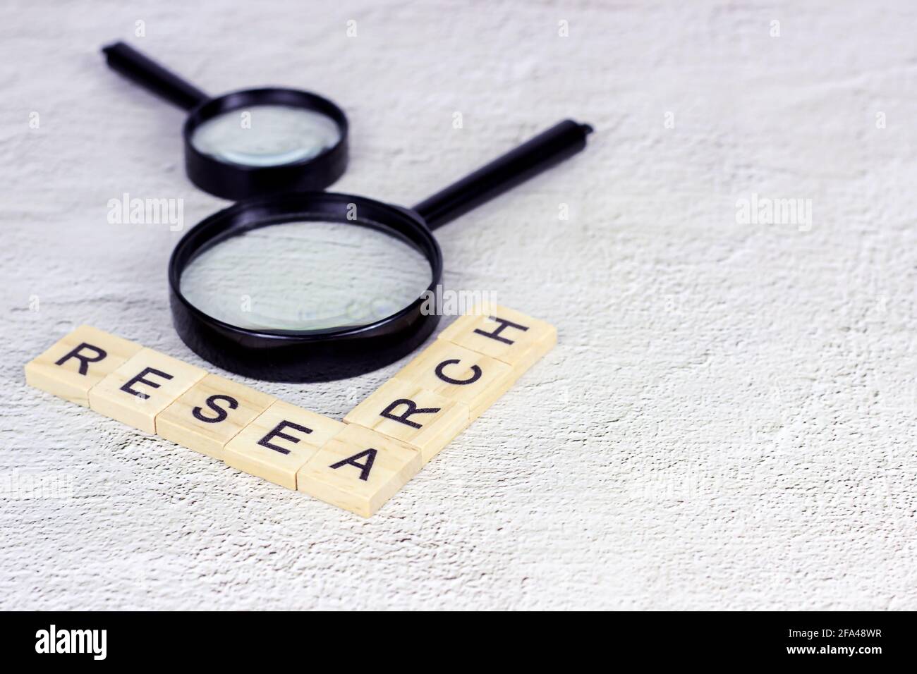 Black magnifying glass with research text on light gray background with ...