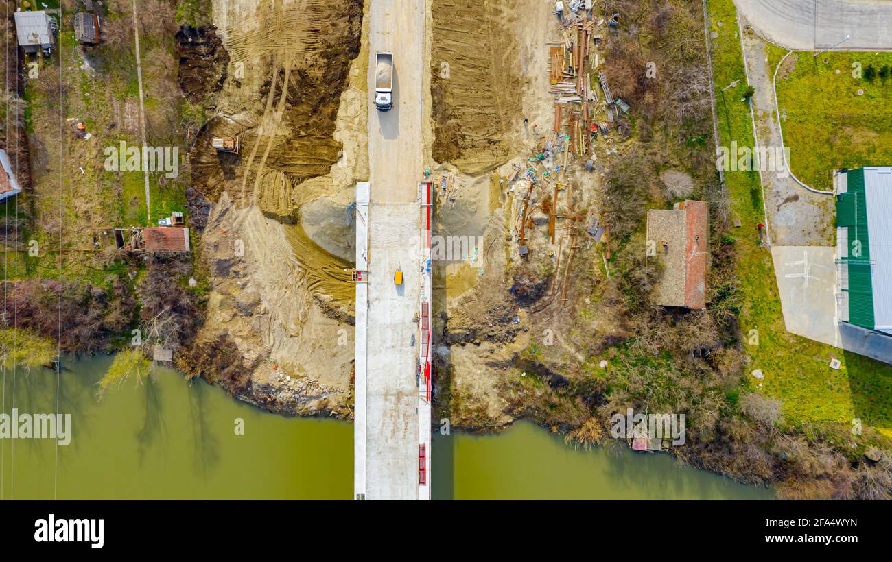 Above top view, overhead, on unfinished bridge, road over river is ...