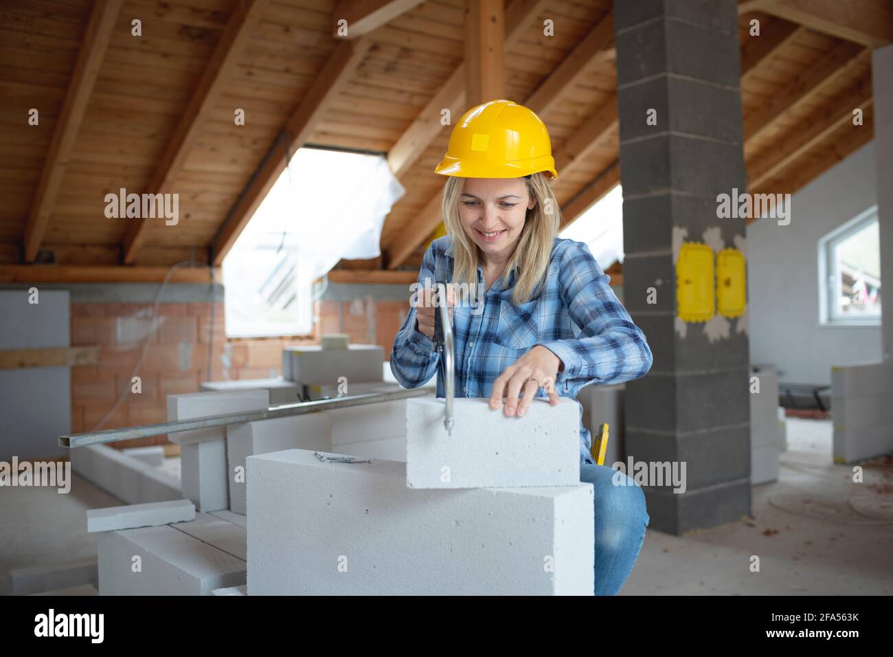 pretty young female bricklayer with yellow safety helmet is sawing ...