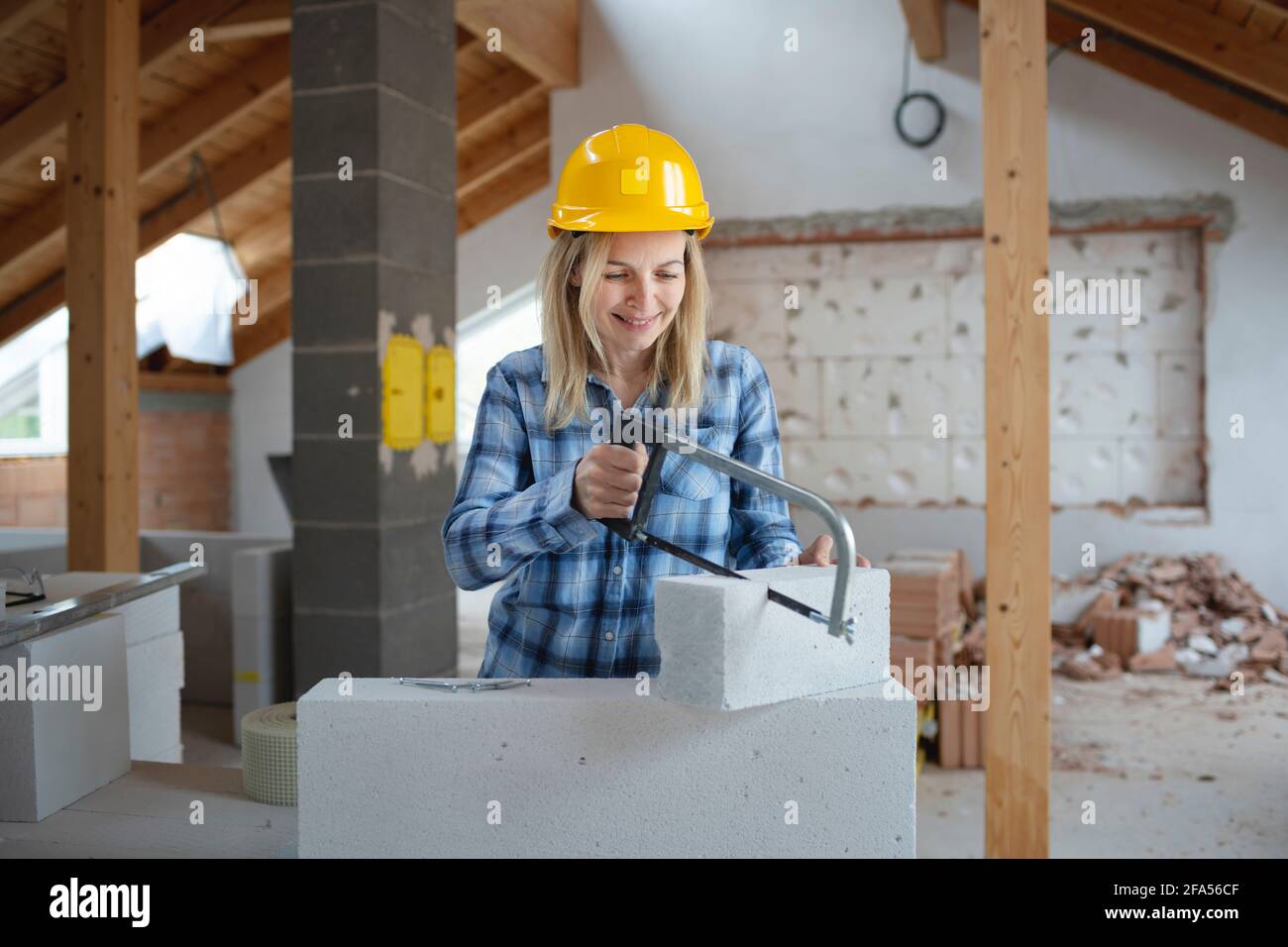 pretty young female bricklayer with yellow safety helmet is sawing ...