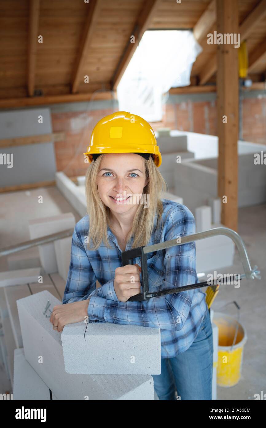 pretty young female bricklayer with yellow safety helmet is sawing ...