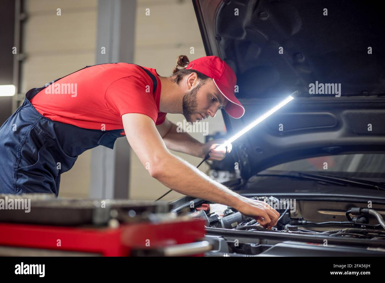 Auto mechanic with lamp near open hood of car Stock Photo - Alamy