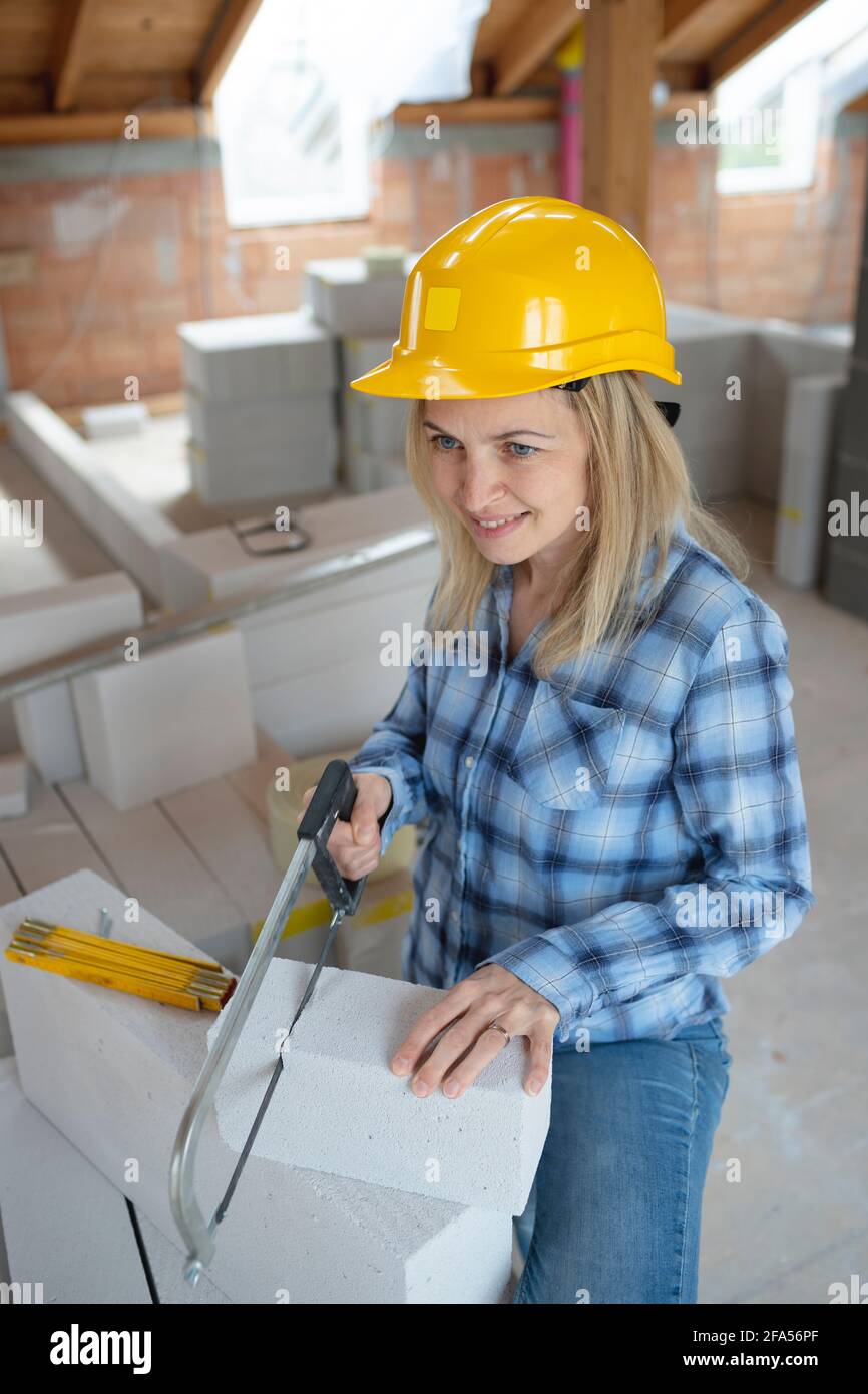 pretty young female bricklayer with yellow safety helmet is sawing ...