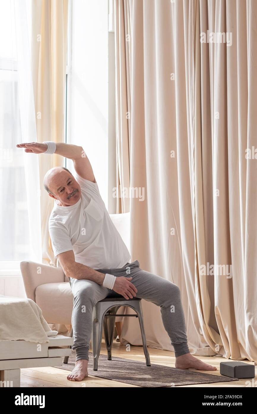 Senior caucasian man stretching side sitting on chair at his living ...