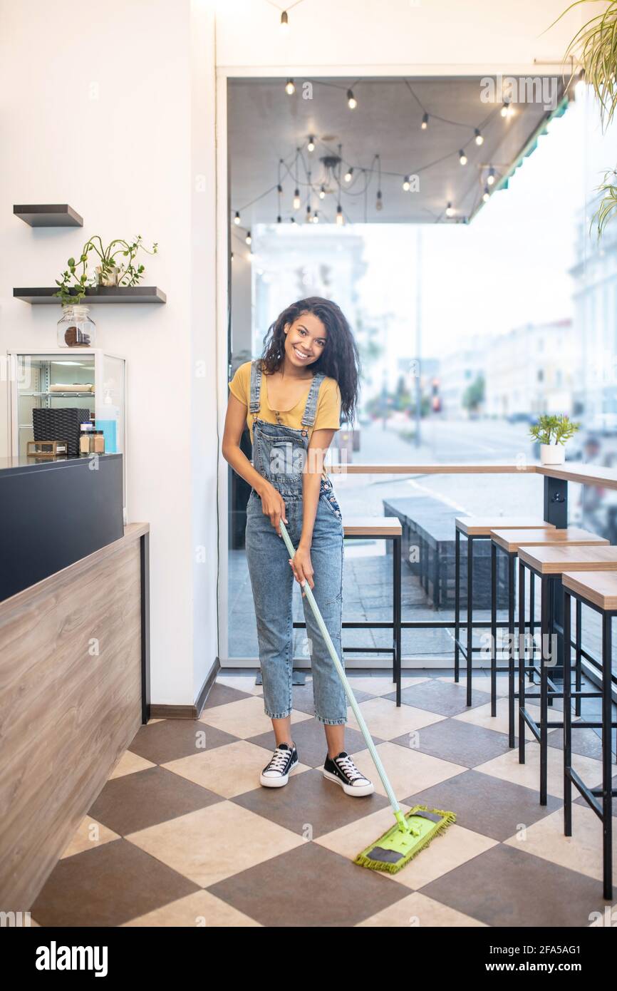 Young woman cleaning cafe in good mood Stock Photo - Alamy