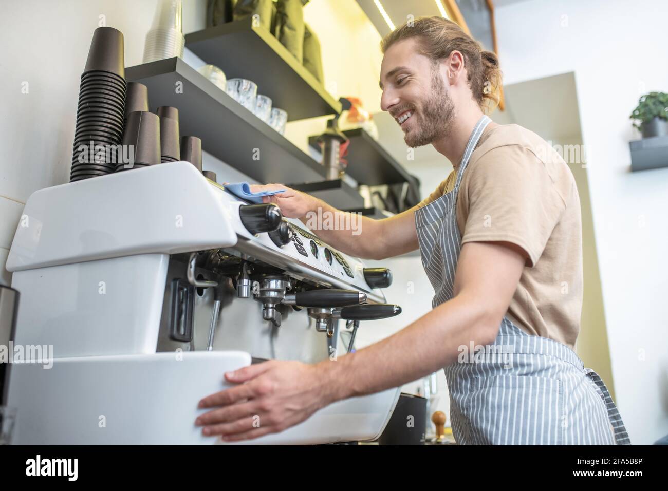 Joyful man in apron wiping coffee machine Stock Photo - Alamy