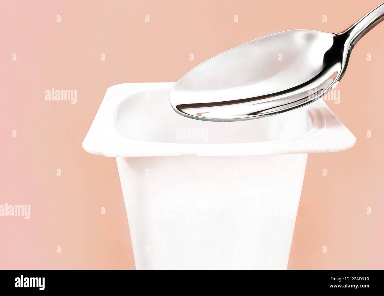 Yogurt cup and silver spoon on beige background, white plastic ...