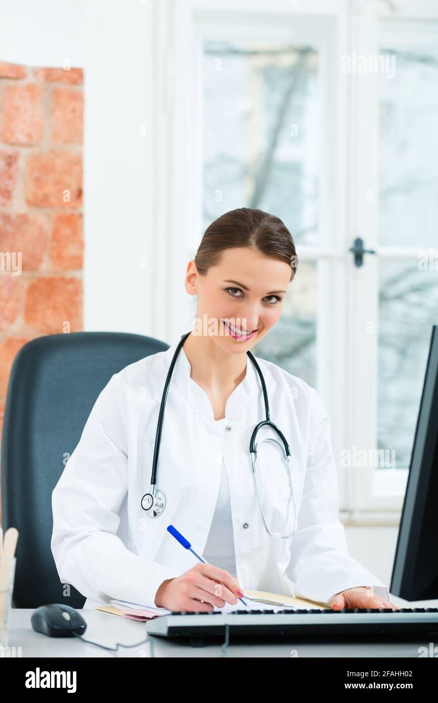 Young female doctor sitting at a desk in front of window in clinic ...