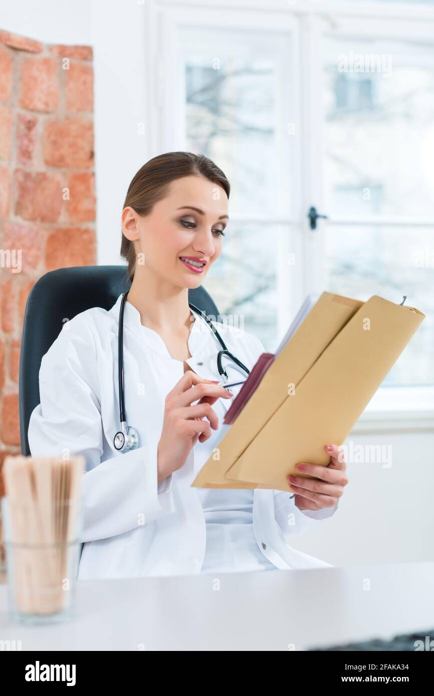 Young female doctor sitting at a desk in front of window in clinic ...