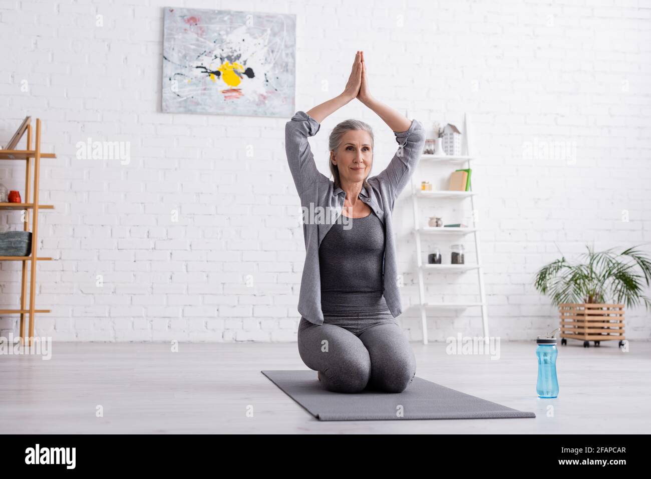 mature woman with grey hair and praying hands above head practicing ...