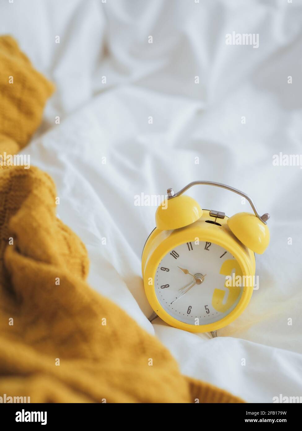 Vertical shot of a yellow alarm clock on a white cloth Stock Photo - Alamy