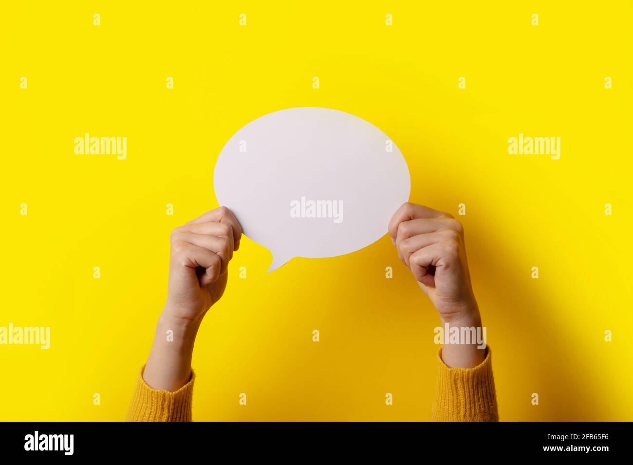 Dialogue icon, blank speech bubble in hand over yellow bacckground ...