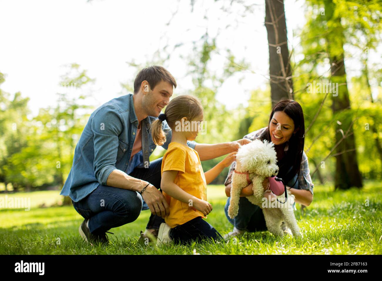 Beautiful happy family is having fun with bichon dog outdoors in the ...