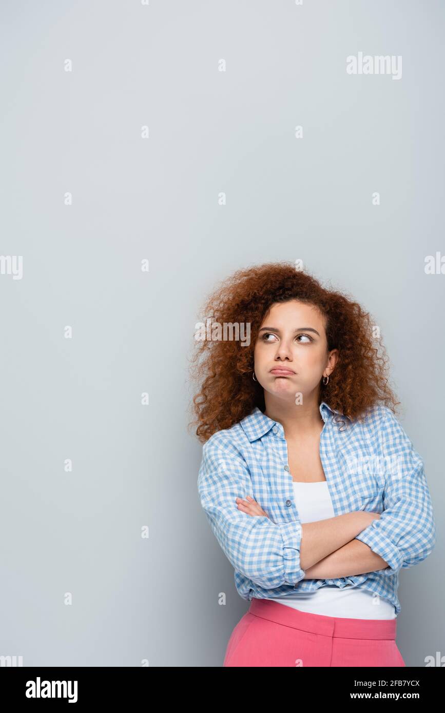upset woman standing with crossed arms and pouting lips on grey ...