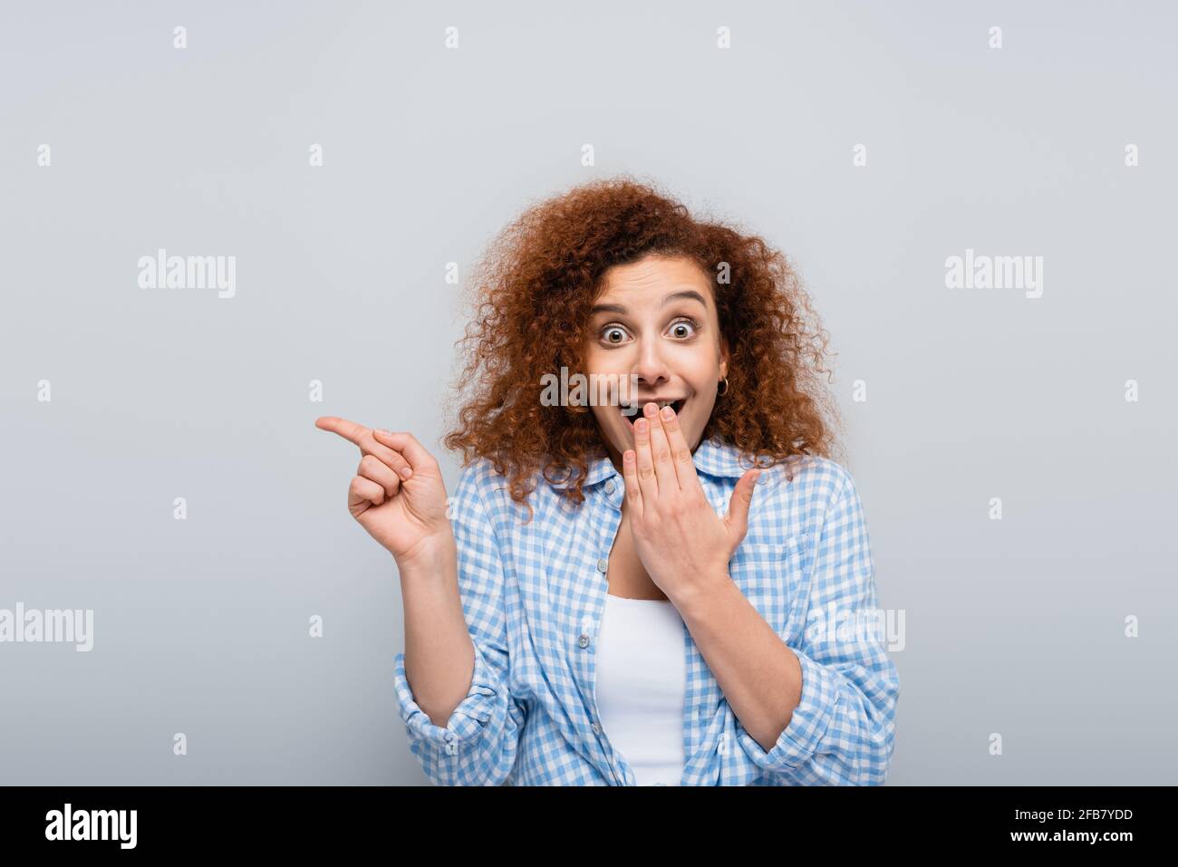 shocked woman pointing with finger and covering mouth with hand ...