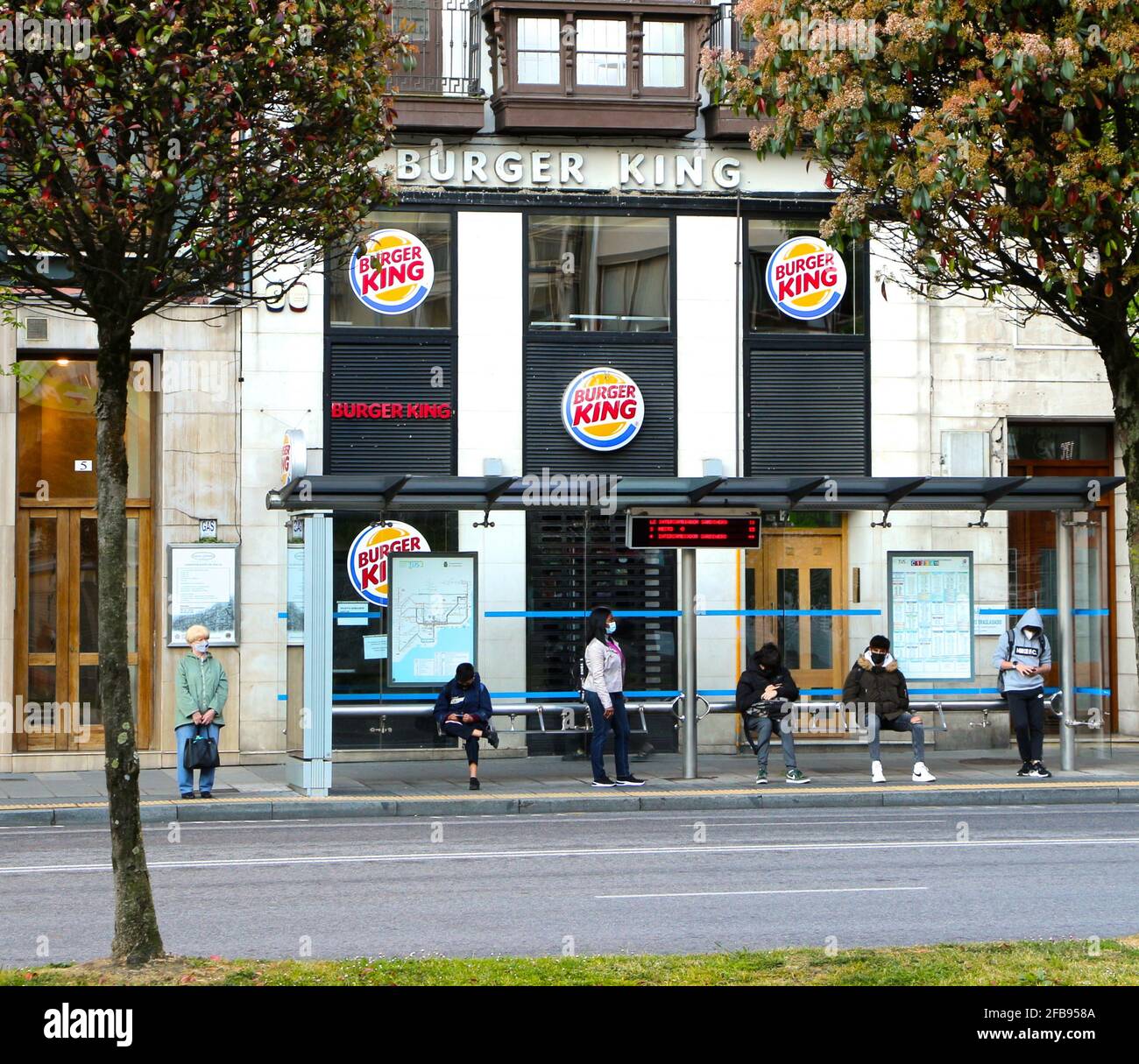 People waiting at a bus stop Early morning closed Burger King fast food ...