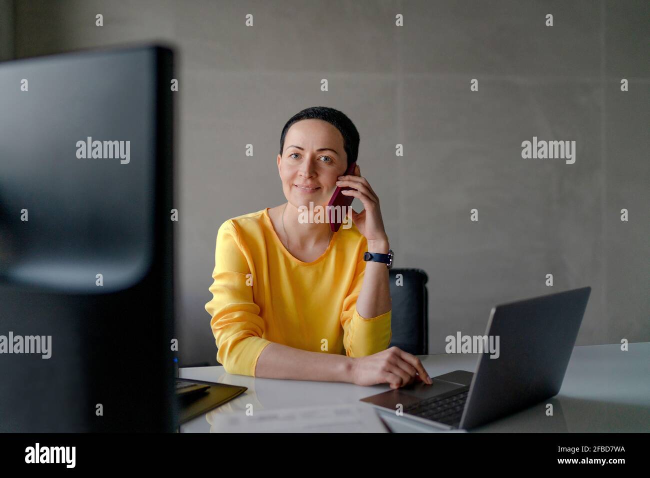 Contented female entrepreneur with laptop talking on mobile phone at ...