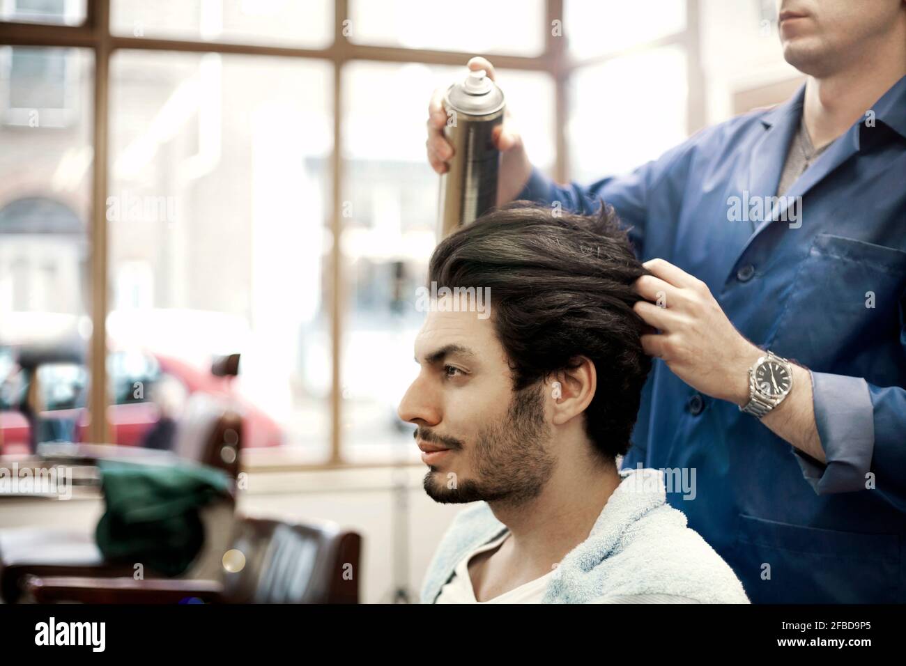 Barber spraying hair of male customer Stock Photo - Alamy