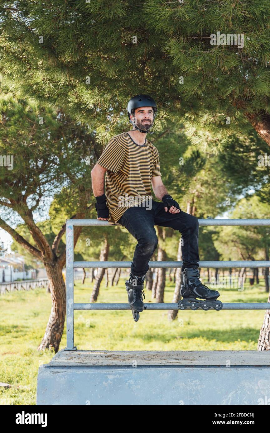 Mid adult man with sports helmet and roller skates sitting on railing ...