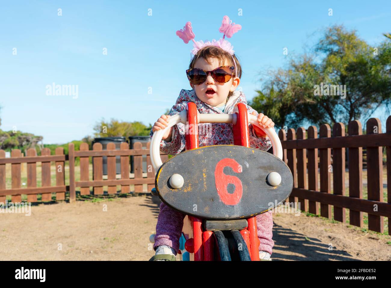 Cute baby girl sitting on motorcycle on playground during sunny day ...