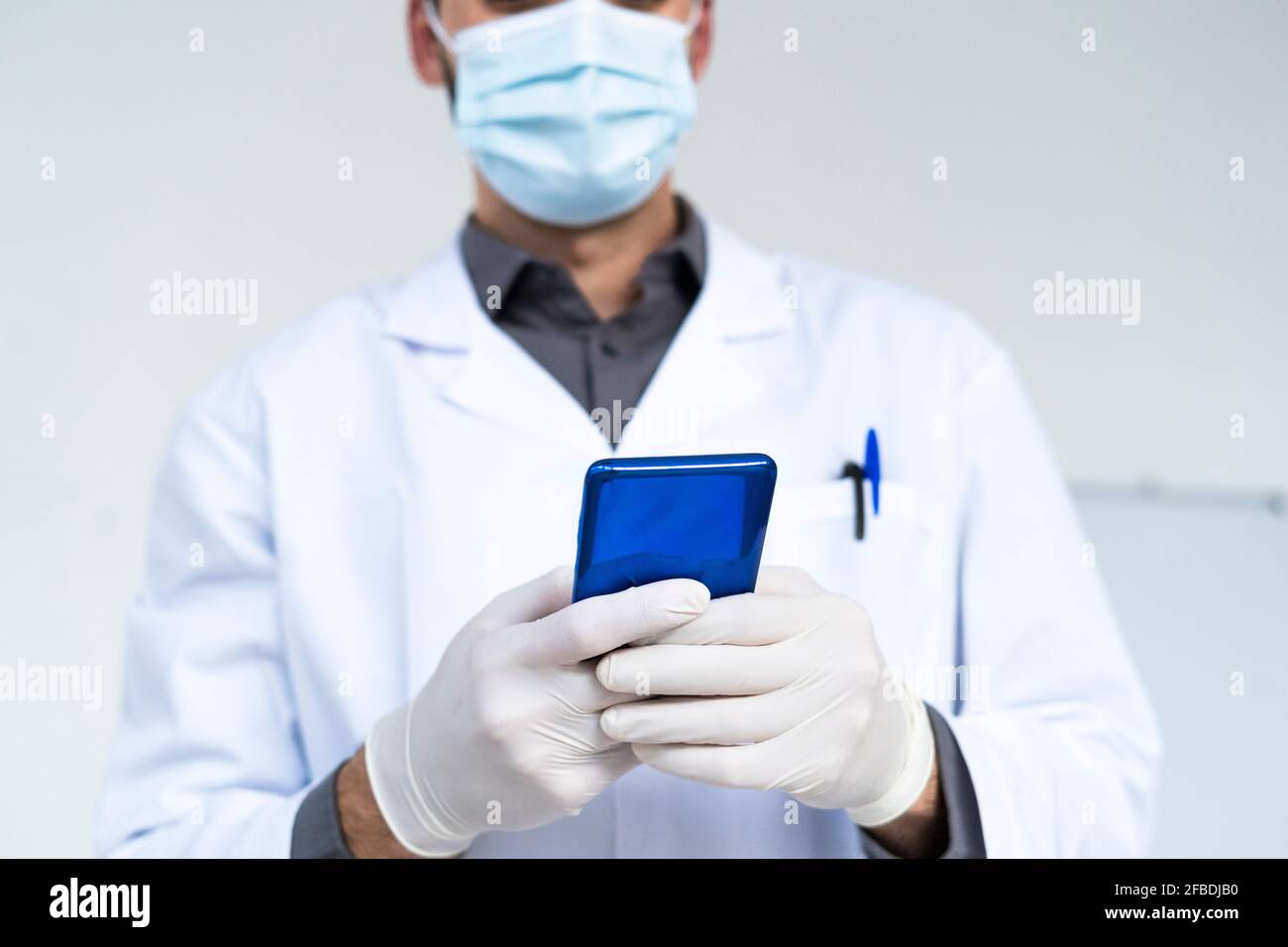 Male doctor text messaging through smart phone in hospital during COVID ...