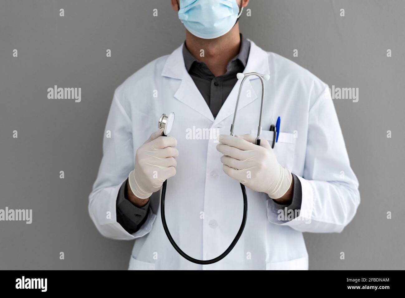Male doctor wearing surgical glove holding stethoscope in front of wall ...