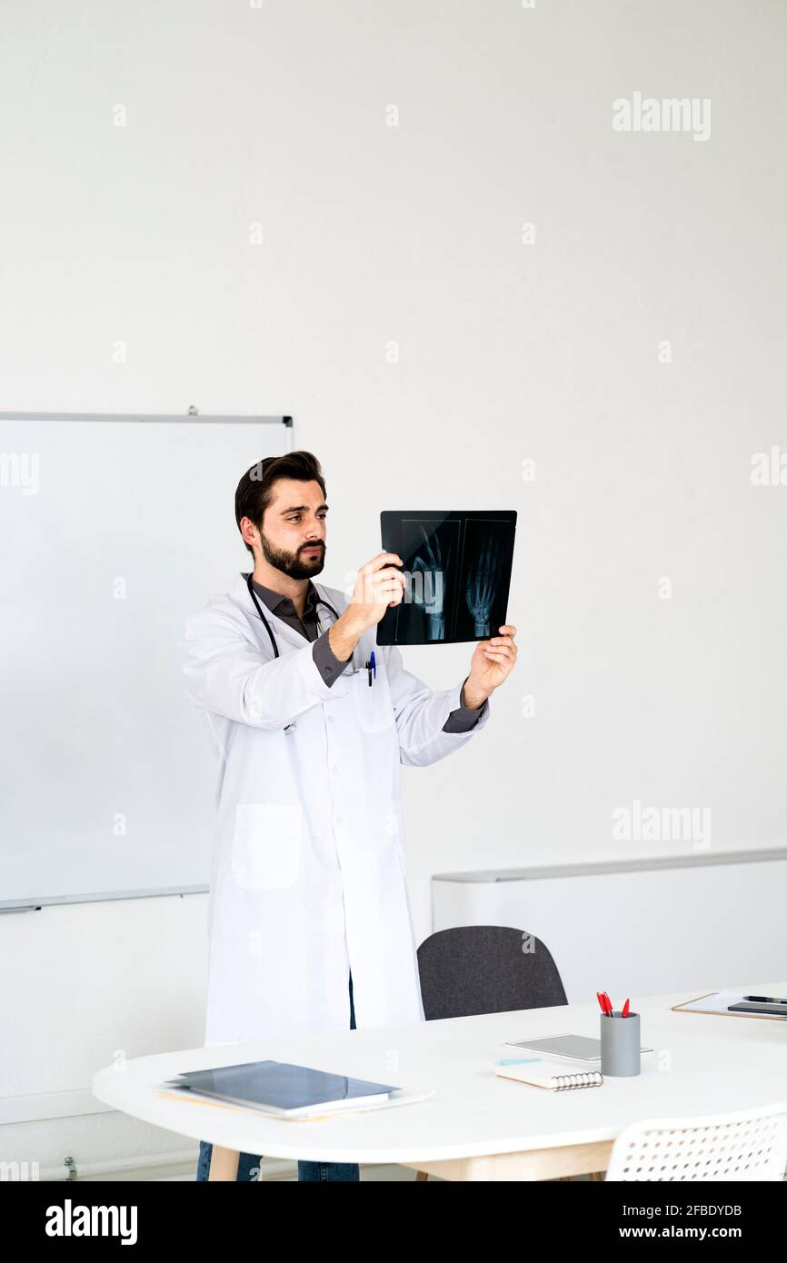 Male doctor analyzing X-ray report while standing at desk in hospital ...