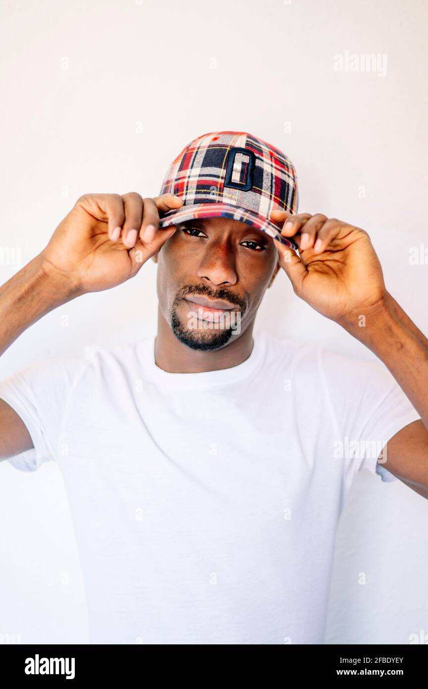 Young man adjusting cap against white background Stock Photo - Alamy