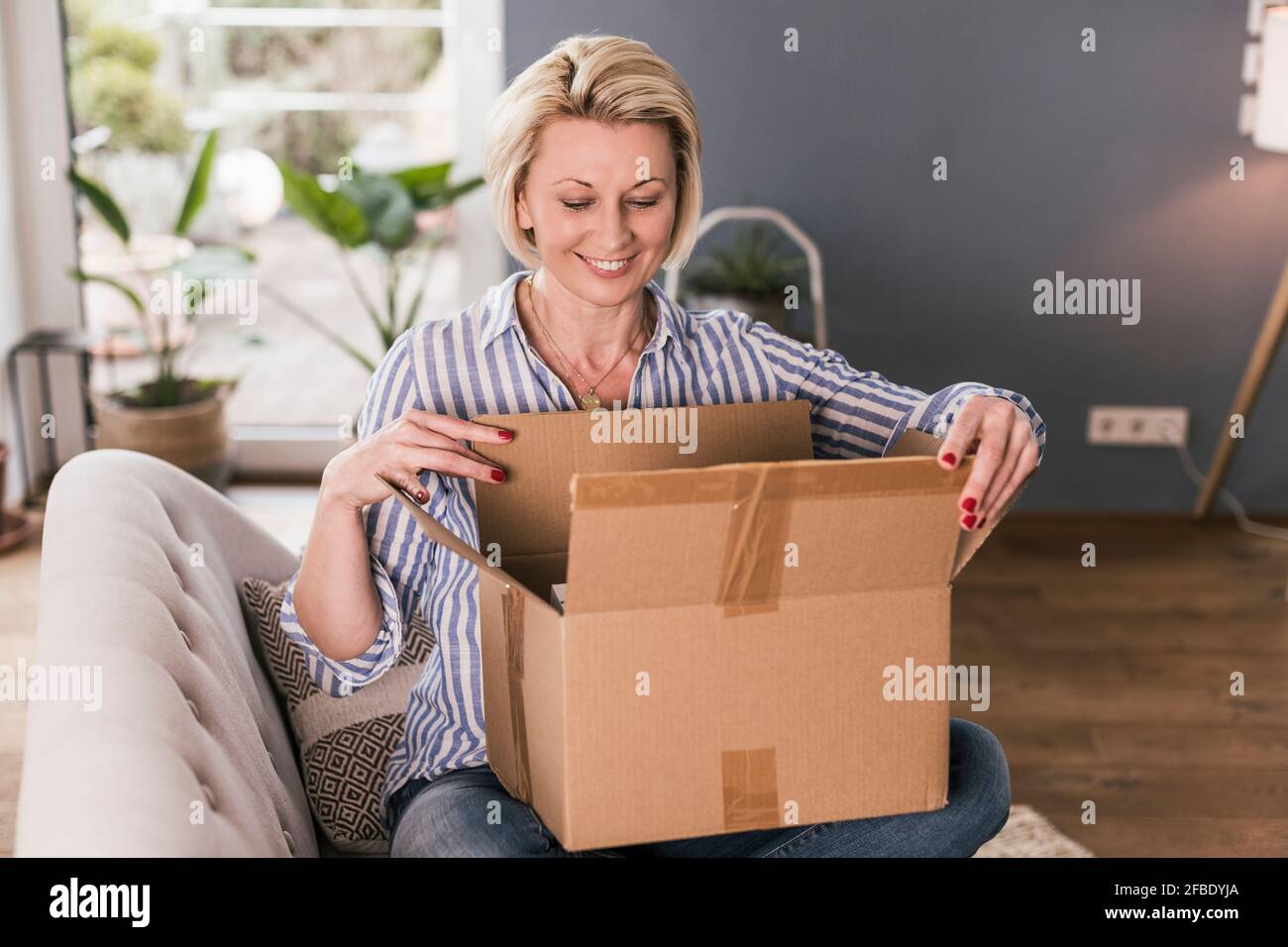 Smiling mature woman opening box at home Stock Photo - Alamy