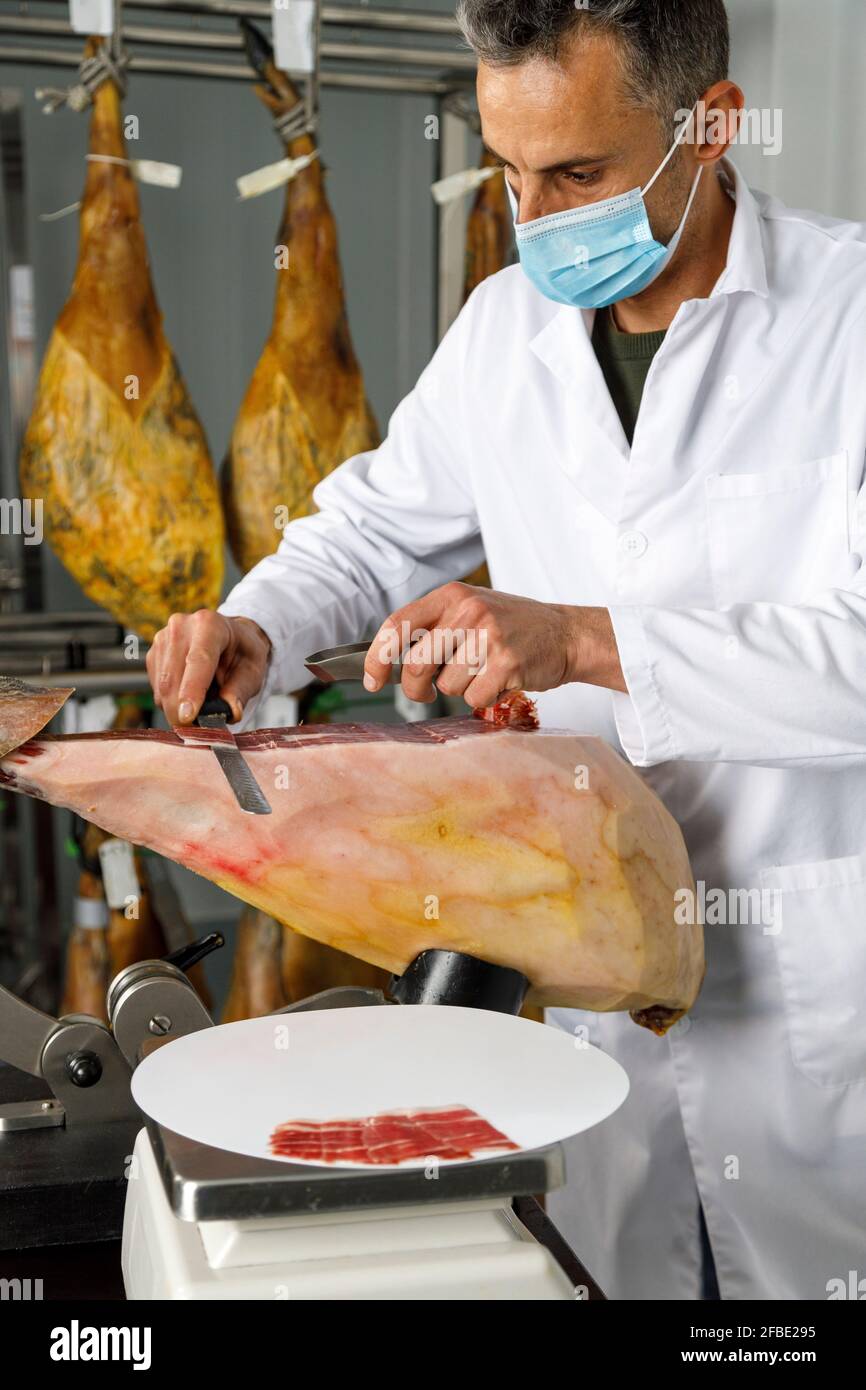 Male butcher cutting ham at shop during pandemic Stock Photo - Alamy