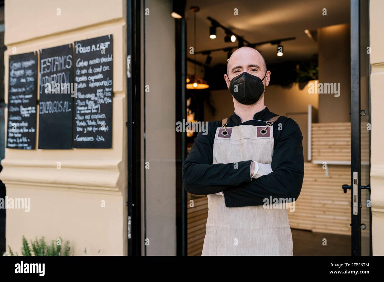 Mature male restaurant owner with arms crossed standing at doorway ...