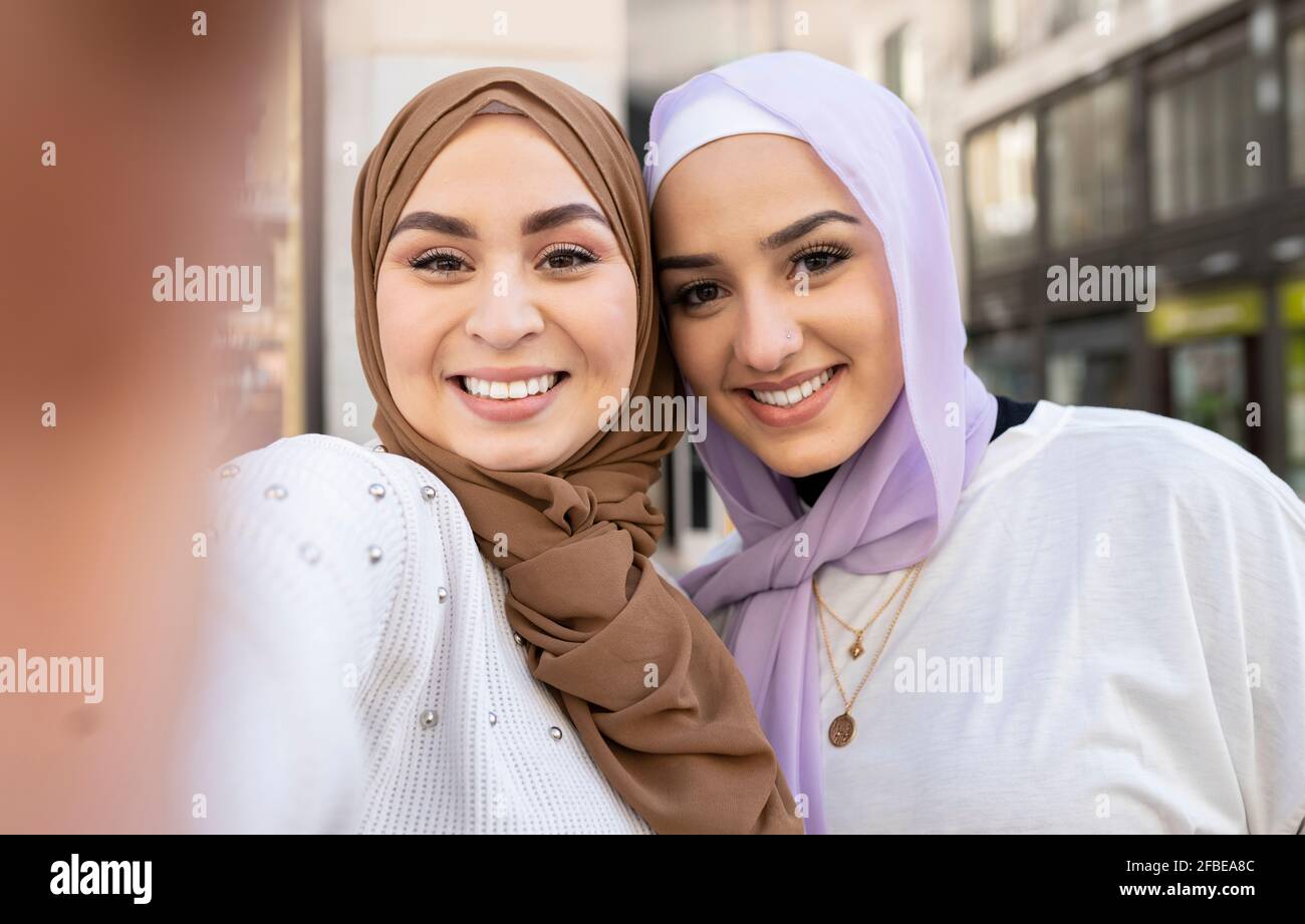 Smiling Arab female friends in hijabs taking selfie in city Stock Photo ...