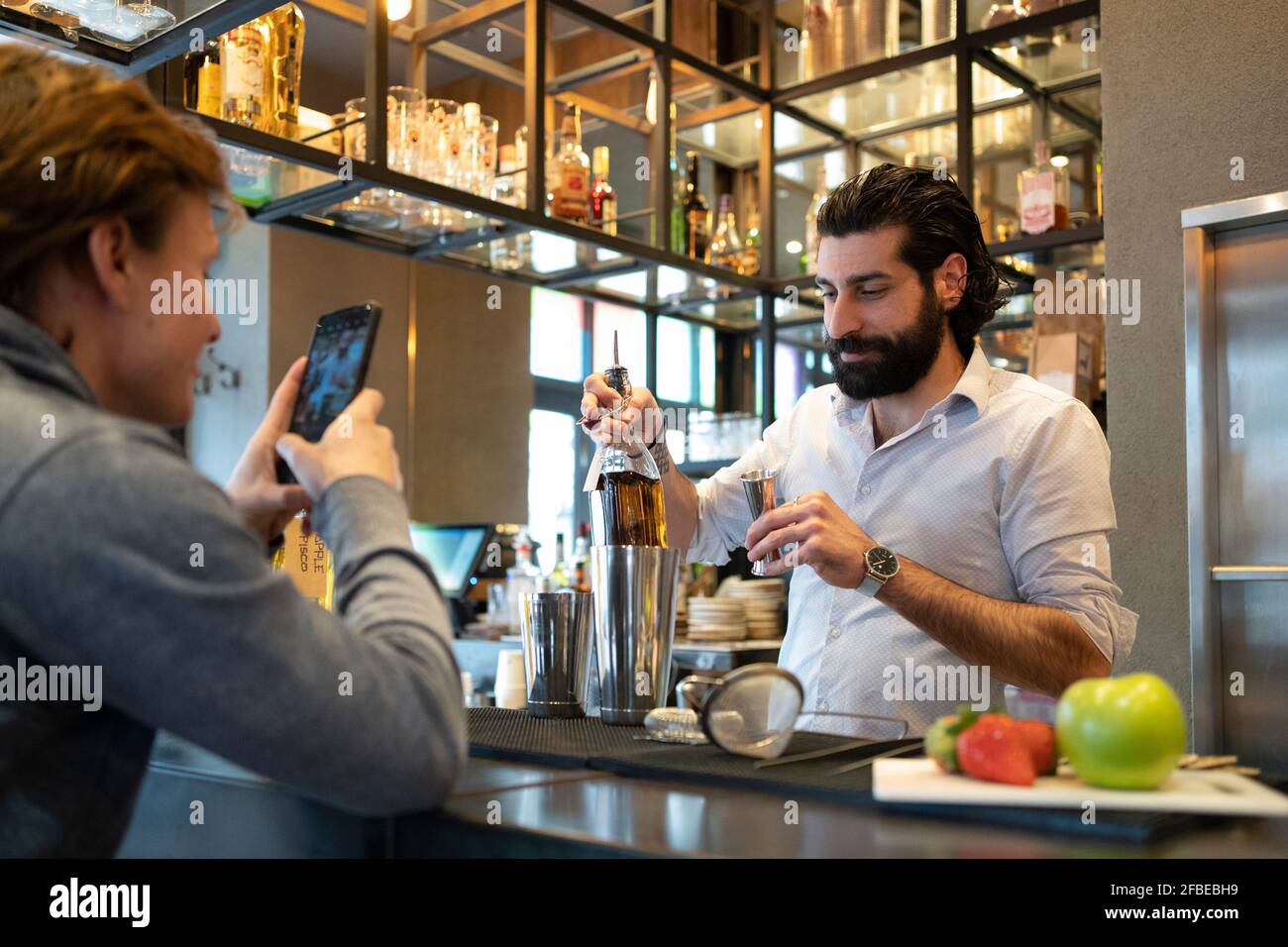 Customer using smart phone while bartender making cocktail at bar ...
