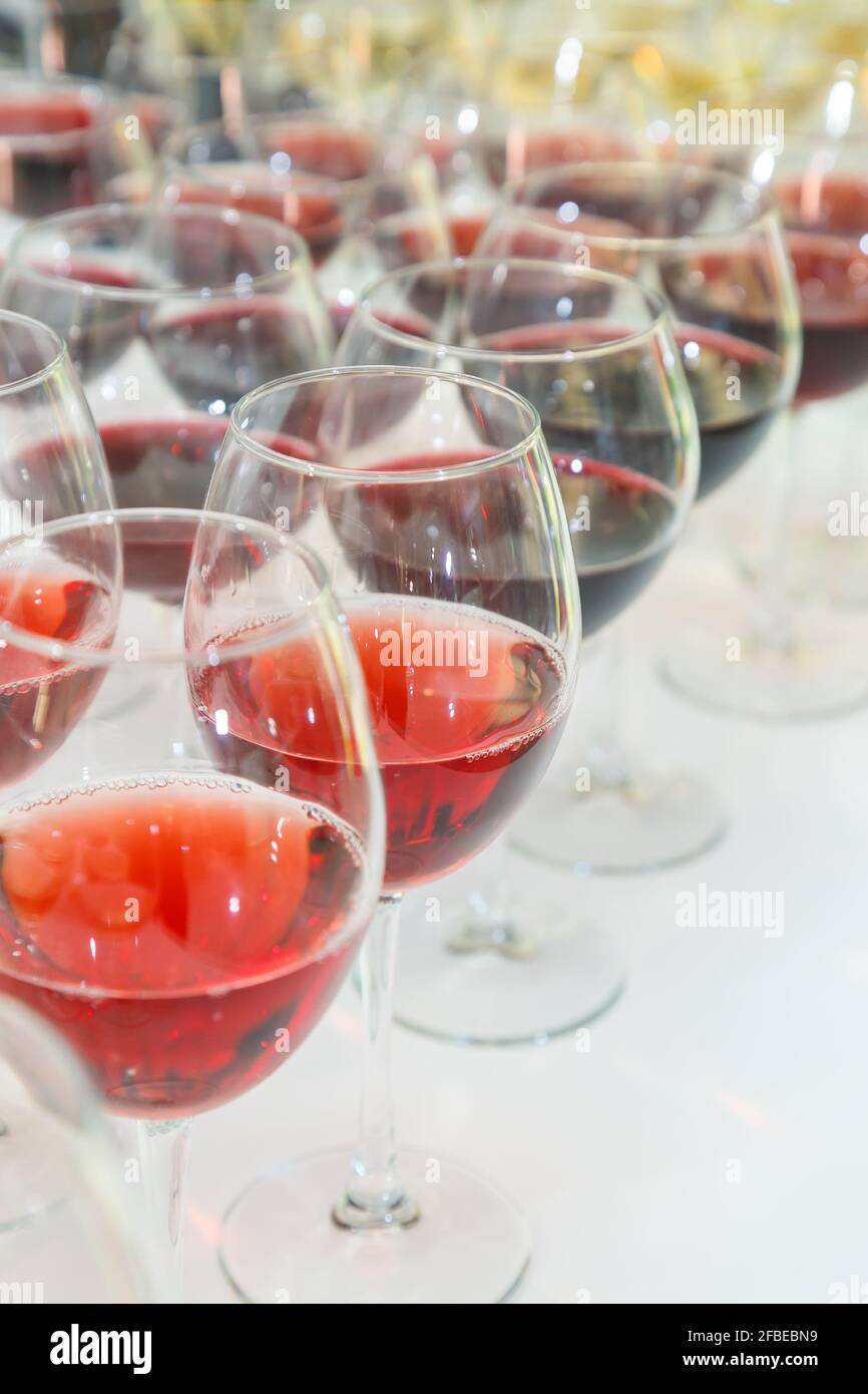 A large number of glass goblets filled with red wine are neatly ...
