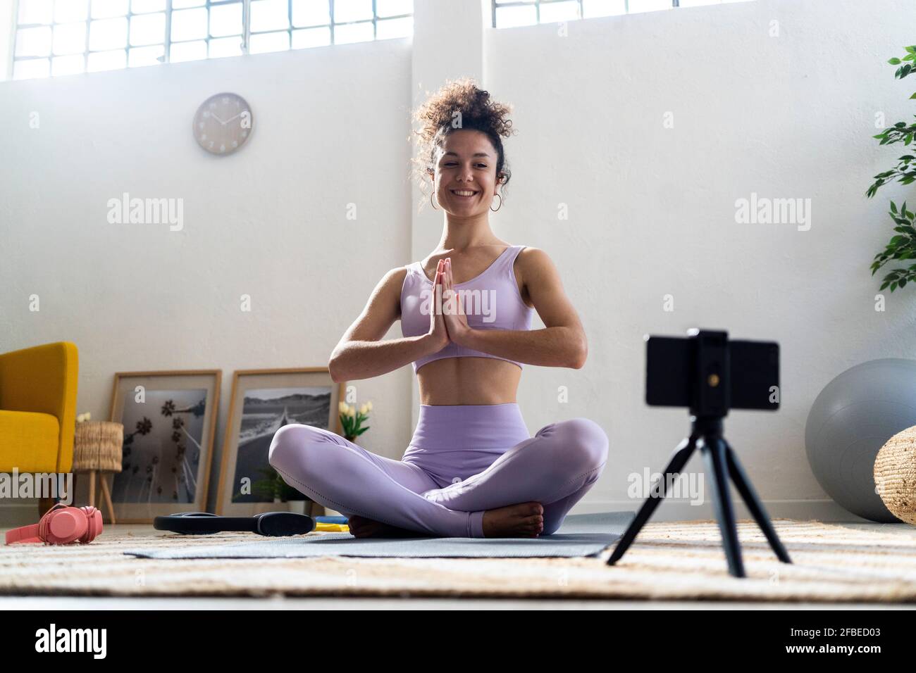 Smiling female influencer with hands clasped vlogging while doing yoga ...